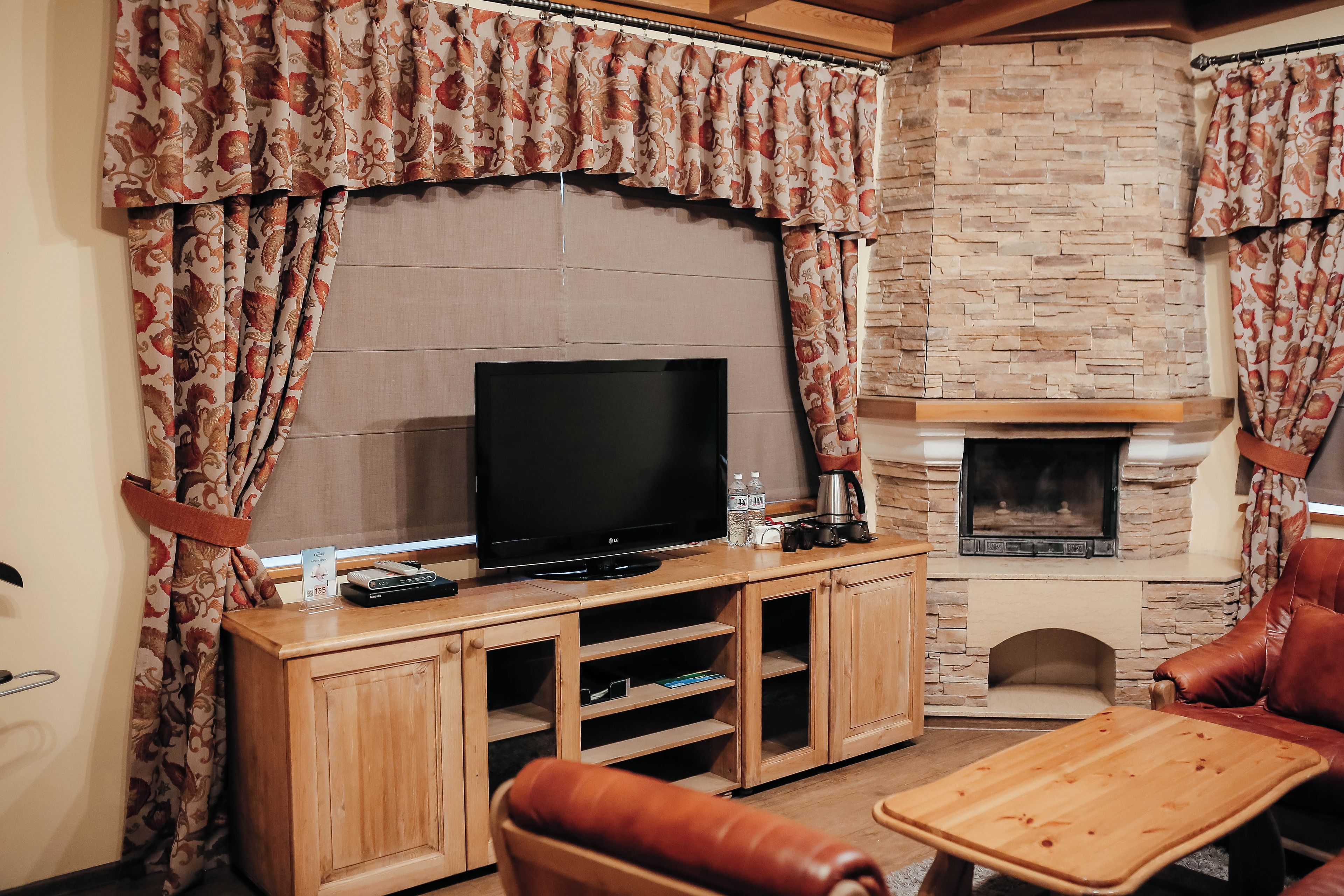 Sala de estar com TV de tela plana, painel de entretenimento em madeira, poltrona de couro e lareira de pedra.