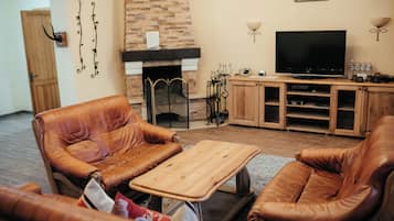 Sala de estar com sofás de couro, mesa de centro de madeira, lareira, televisão e um armário com diversos objetos.