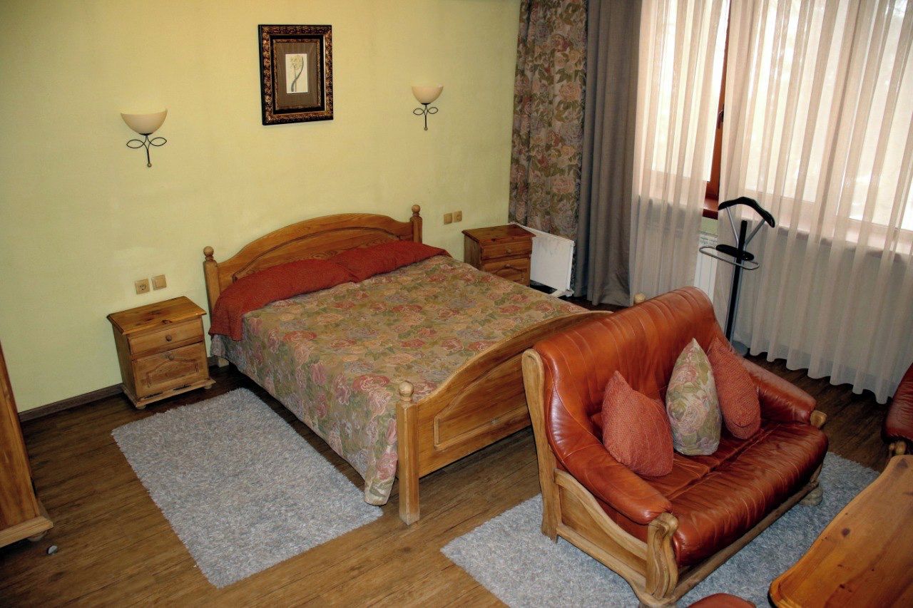 Quarto com cama de madeira, sofá de couro, mesa de cabeceira e luminária na parede.