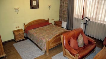 Quarto com cama de madeira, sofá de couro, mesa de cabeceira e luminária na parede.