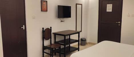 Quarto com uma cama, escrivaninha, cadeira, televisão e ventoinha no teto.