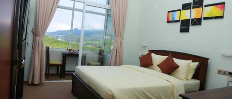 Quarto de hotel com uma cama, uma secretária e vista para uma paisagem verde pela janela.
