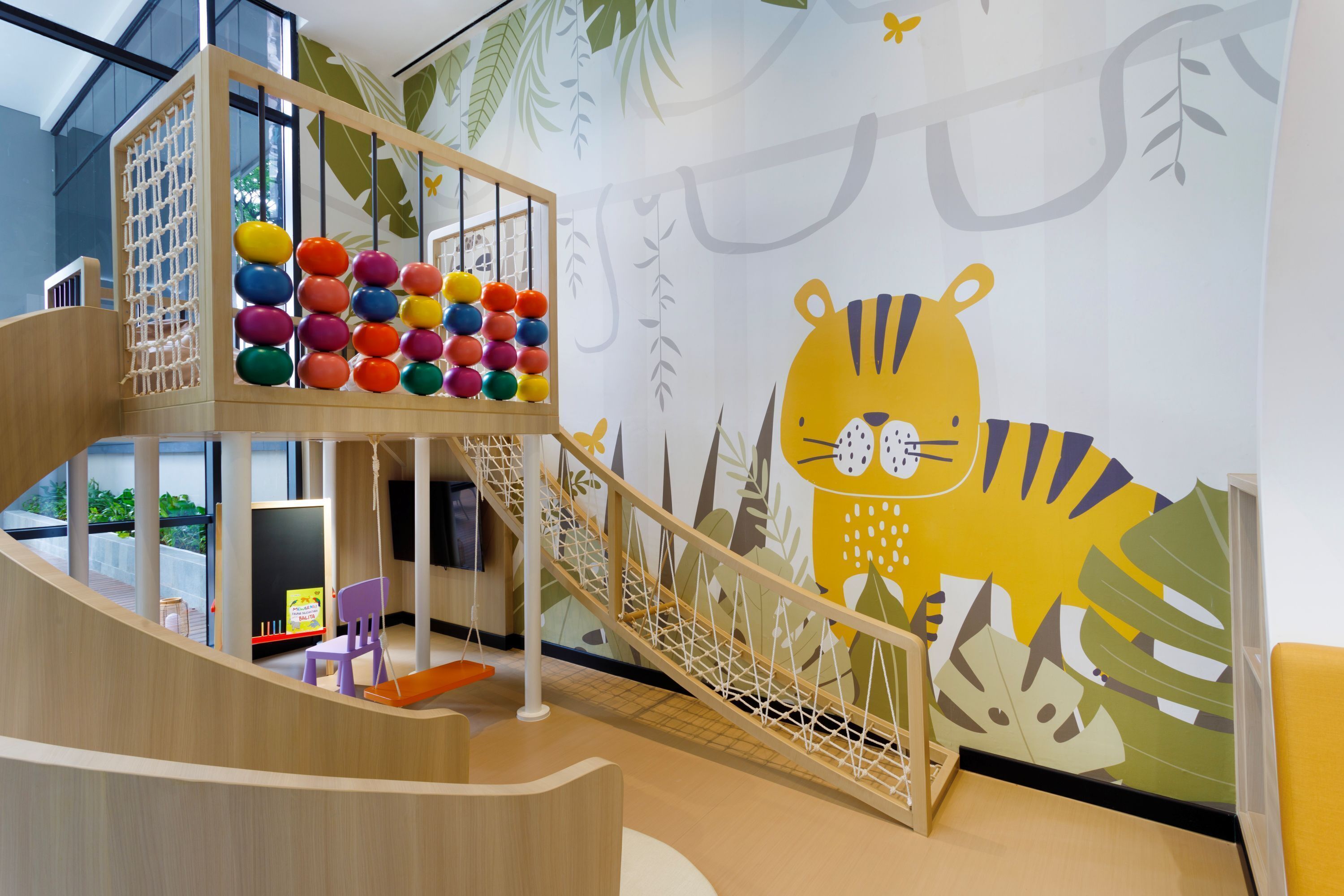 Espaço infantil com um muro de bolas colorido, um escorrega e um mural de um tigre.