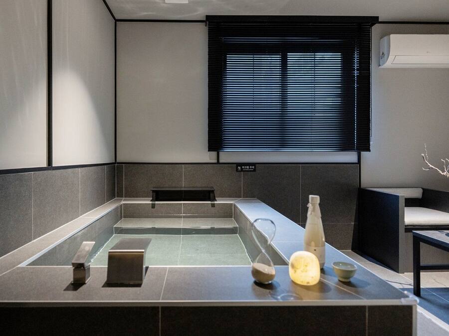 Uma sala de spa moderna com uma banheira de hidromassagem, um banco e uma pequena mesa com objetos decorativos.