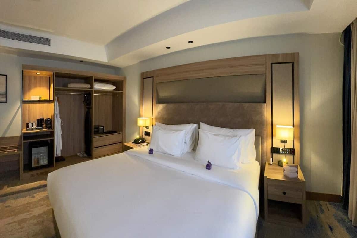 Quarto de hotel com uma cama grande, mesas de cabeceira com luminárias, guarda-roupa e escrivaninha com cadeira.