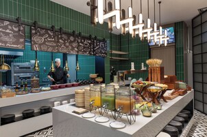 Buffet com diversas opções de comida e bebidas, um chef trabalhando e uma cozinha moderna ao fundo.