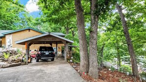 Uma cabana de tronco com garagem coberta e uma entrada de automóveis que leva a um SUV preto.