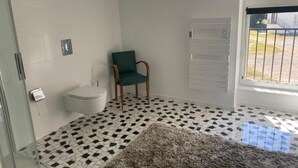 Um banheiro com piso ladrilhado, vaso sanitário, cadeira e janela com vista.