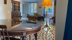 Uma sala de jantar com uma mesa redonda, cadeiras, um armário e um abajur.