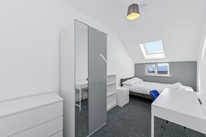 Quarto moderno e bem iluminado, com claraboia, escrivaninha e cama.