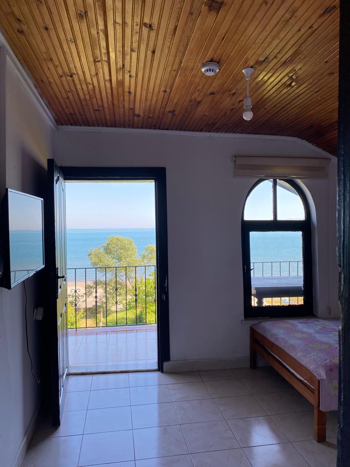 Quarto com teto de madeira, cama, televisão e varanda com vista para o mar.