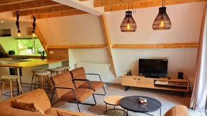 Uma sala de estar acolhedora com sofá, cadeiras, mesa de centro, televisão e área de cozinha com banquetas.