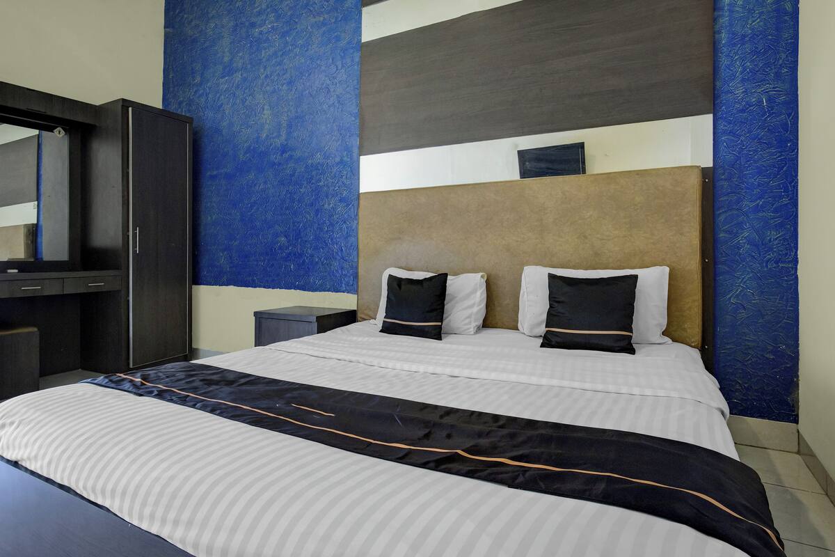 Quarto de hotel com uma cama grande, um guarda-roupa, uma mesa de cabeceira e um espelho.