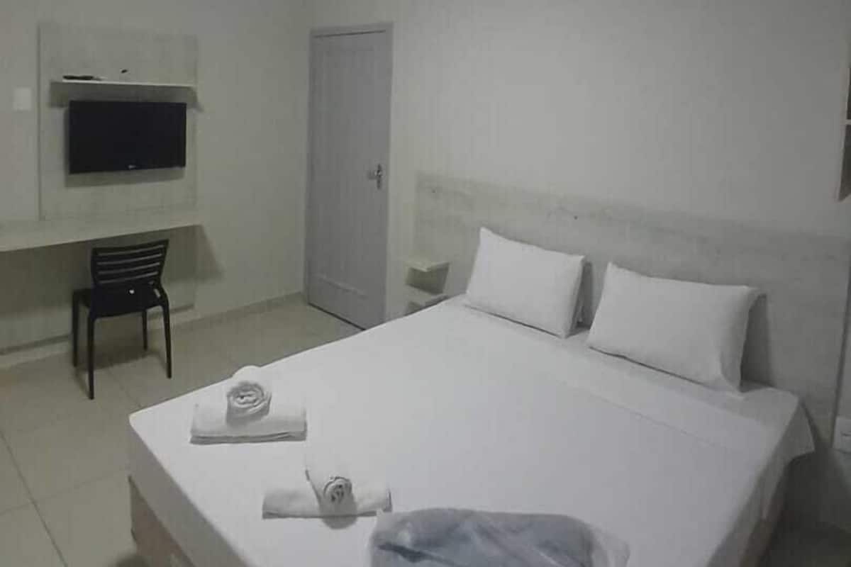 Quarto de hotel com cama, televisão, cadeira e porta.