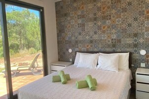Quarto com parede estampada, cama com roupa de cama branca e vista para o exterior.