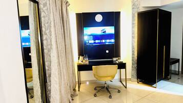 Quarto de hotel com escrivaninha, cadeira, televisão, guarda-roupa e espelho.