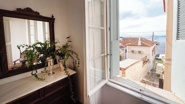 Quarto com um espelho grande, um vaso com plantas e vista para a área costeira através de uma janela aberta.