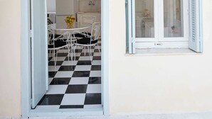 Uma porta dá acesso a um quarto com piso xadrez, uma mesa com cadeiras e um lustre.