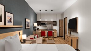 Quarto de hotel moderno com cama, escrivaninha, bancada de cozinha e TV.