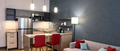 Uma cozinha moderna com ilha central, área de jantar com cadeiras vermelhas e sala de estar com sofá e mesa de centro.