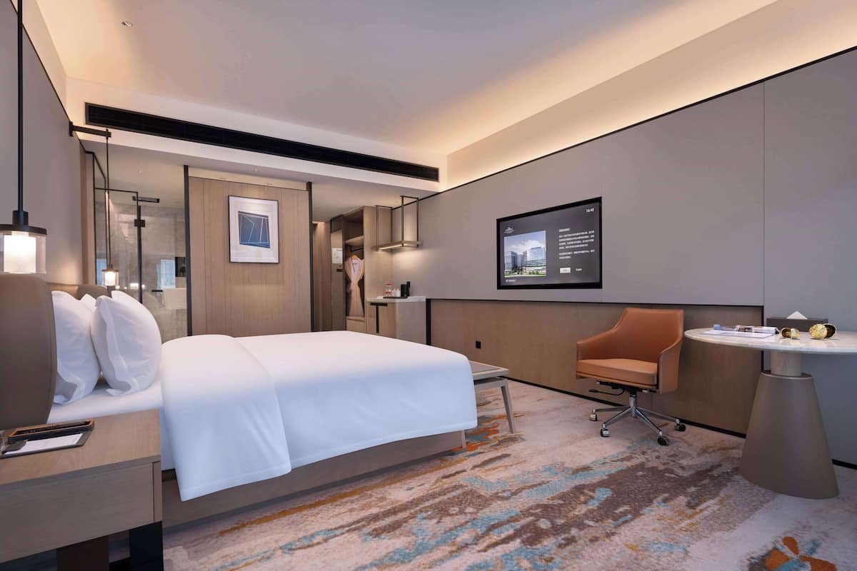 Quarto de hotel moderno com uma cama grande, uma escrivaninha, uma cadeira e uma pequena mesa.