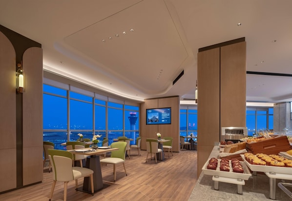 Uma sala de jantar moderna com grandes janelas, uma televisão de tela plana e um buffet com doces.