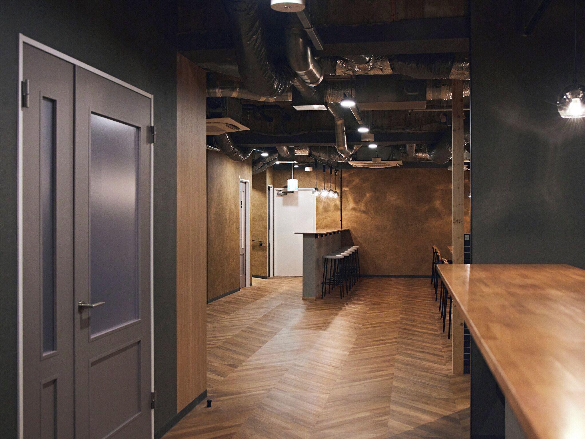 Um interior moderno com um chão de madeira em padrão herringbone, uma área de bar e um espaço de estar.