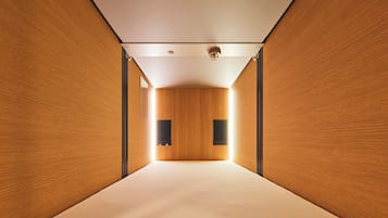 Quarto de hotel moderno e estreito, com paredes de madeira, uma cama e dois alto-falantes fixados na parede.