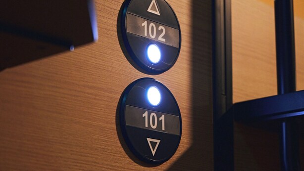 Um conjunto de botões de elevador com os números 102 e 101, cada um com uma seta indicando a direção.