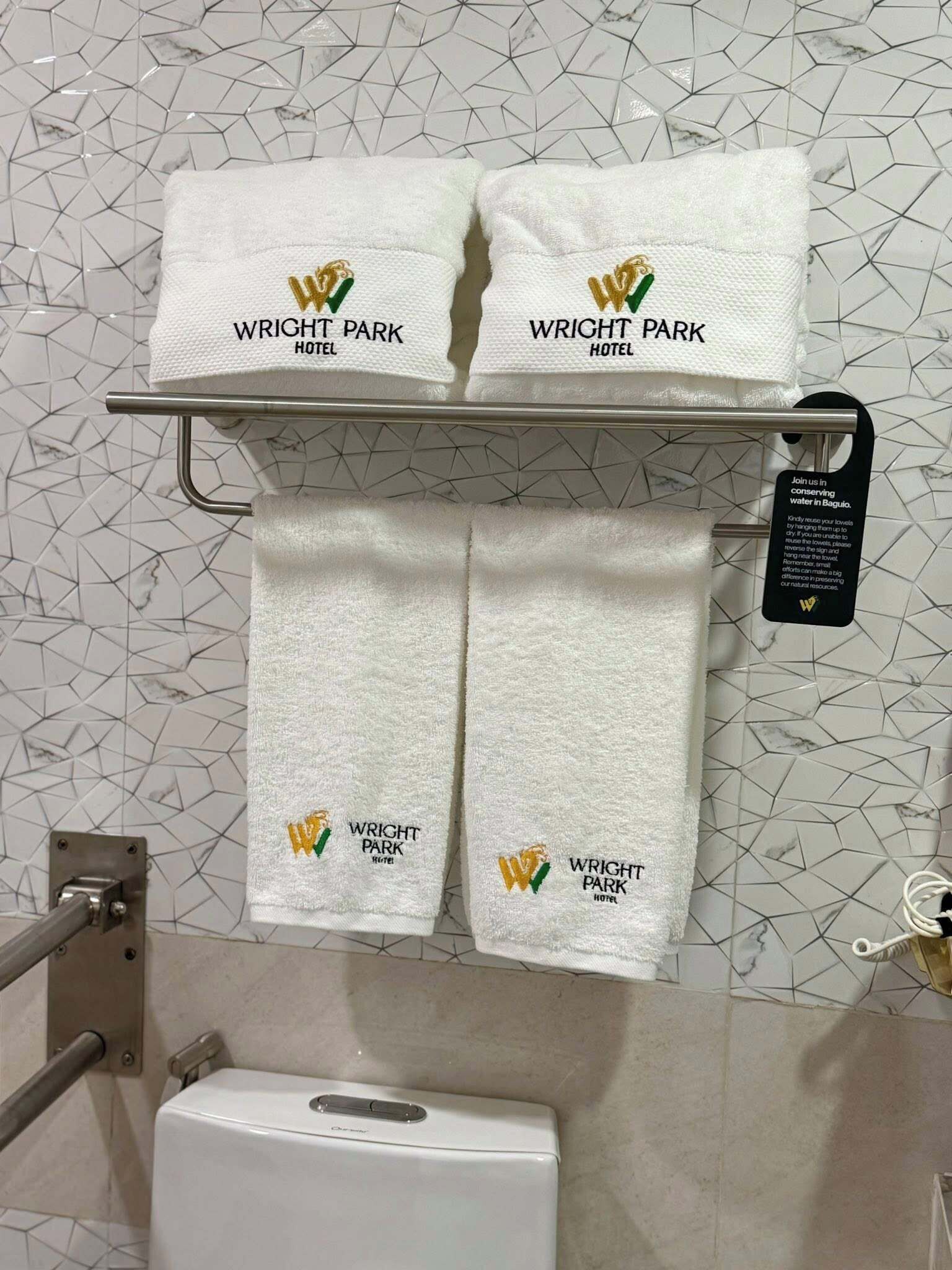 Casa de banho com sanita, um porta-toalhas com duas toalhas e um aviso sobre poupança de água.