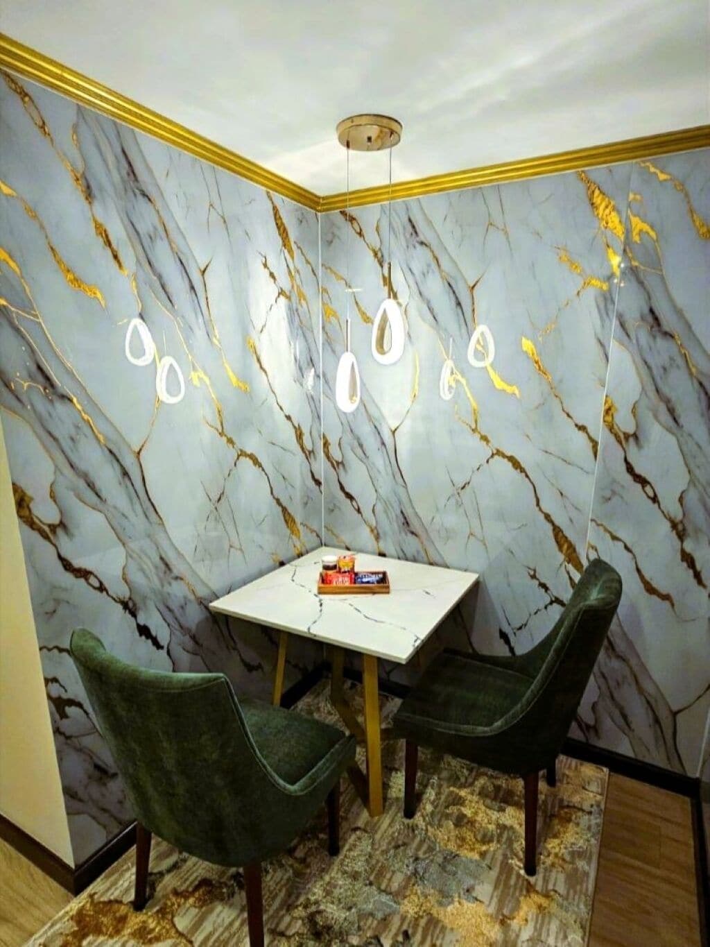 Quarto de canto com parede estampada em mármore, uma pequena mesa com cadeiras e um lustre.