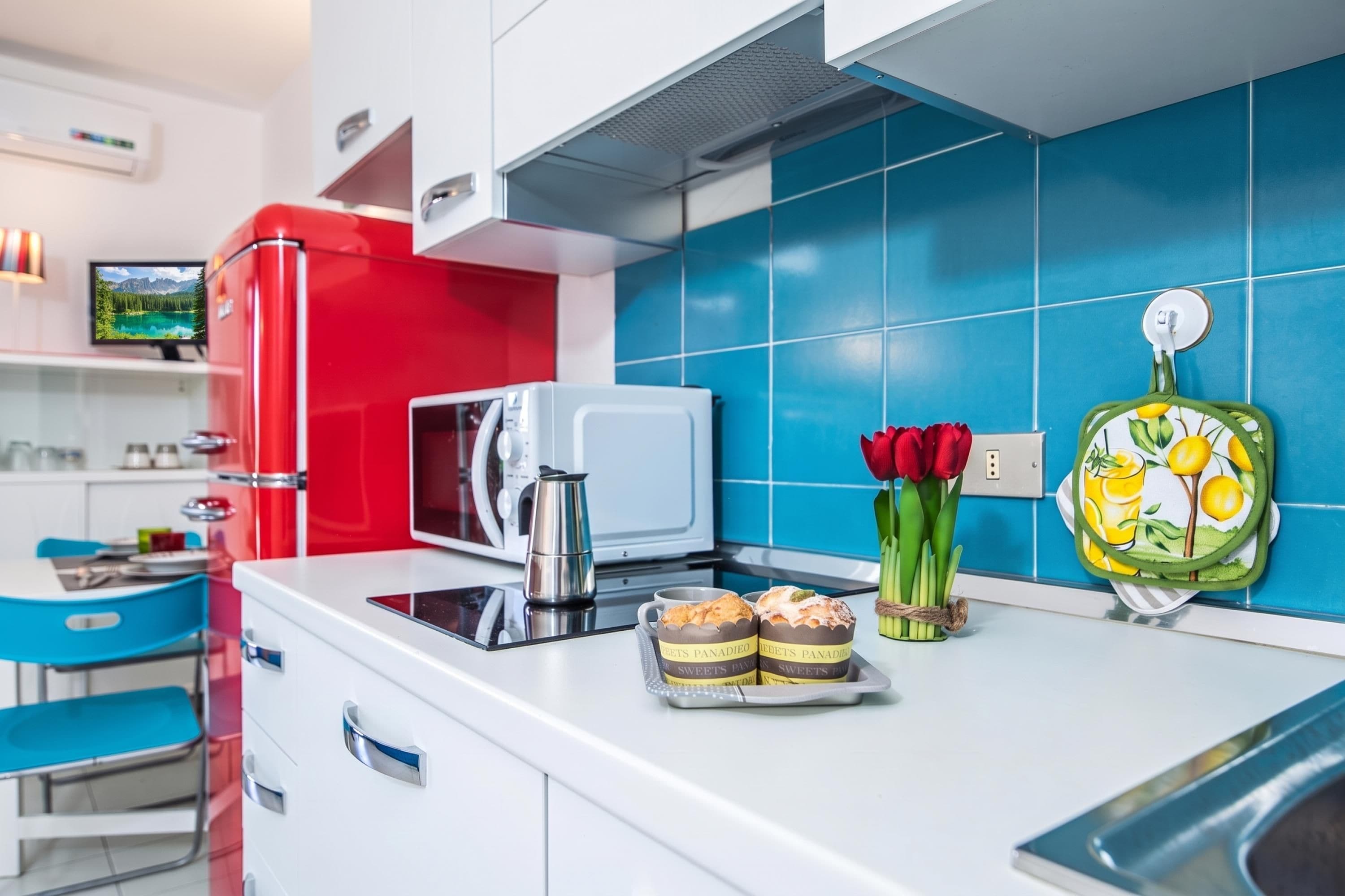 Uma cozinha moderna com uma geladeira vermelha, um micro-ondas branco e um backsplash de azulejos azuis.