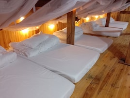 Fileira de camas de madeira com lençóis brancos, cobertas por um dossel branco.