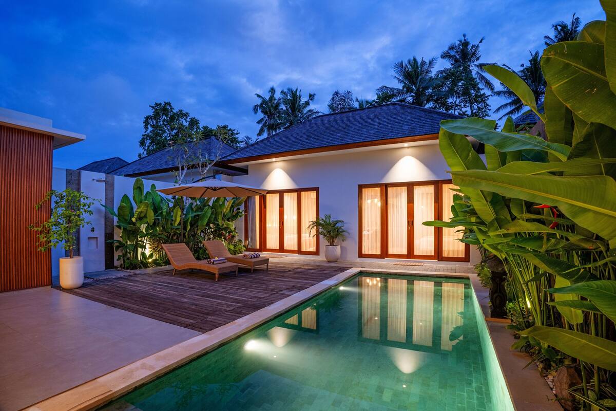 Uma casa moderna com piscina, deck de madeira e plantas tropicais.