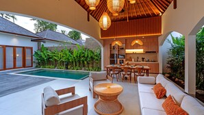 Uma área externa moderna com piscina, móveis de madeira e uma cozinha ao fundo.