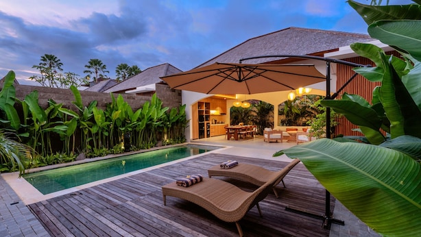 Uma área na beira da piscina com espreguiçadeiras e um terraço coberto.