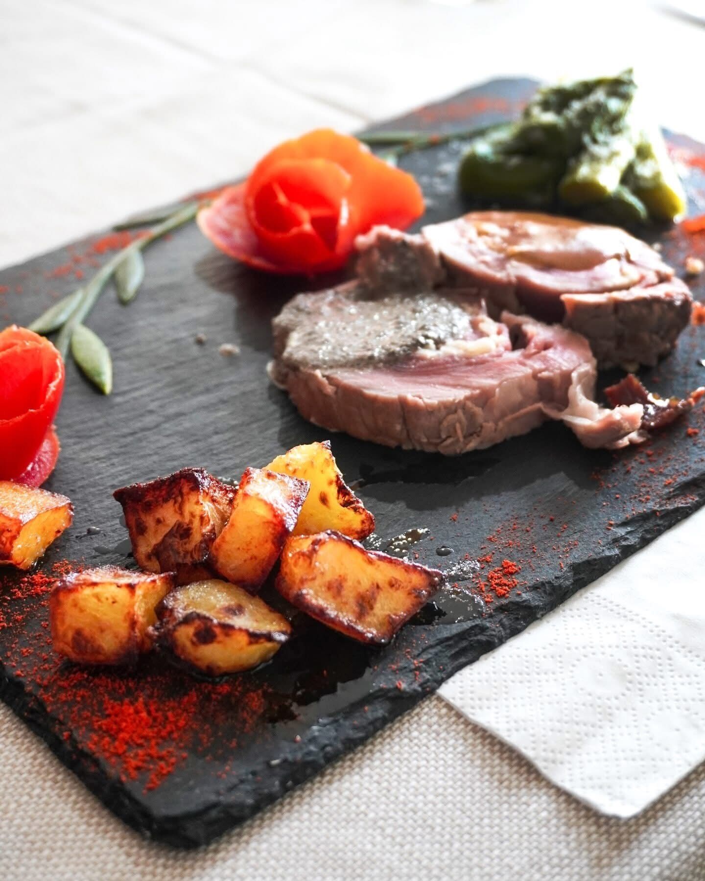 Uma refeição com carne fatiada, batatas assadas e legumes em uma tábua de ardósia.