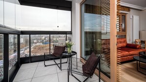 Uma varanda com vista para um canteiro de obras, um sofá, uma mesa com cadeiras e um vaso de flores.