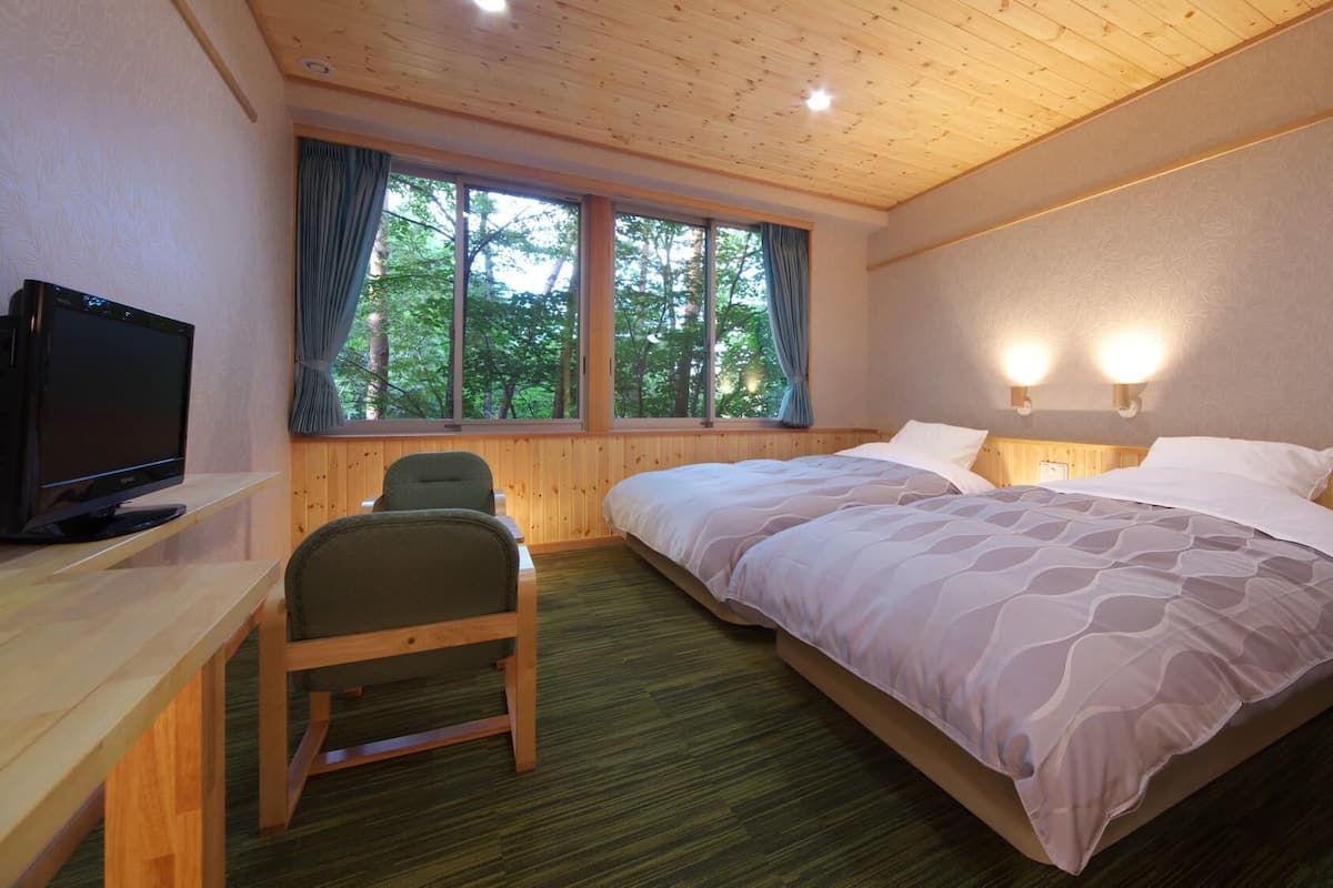 Quarto com cama, cadeira, televisão e janela com cortinas.