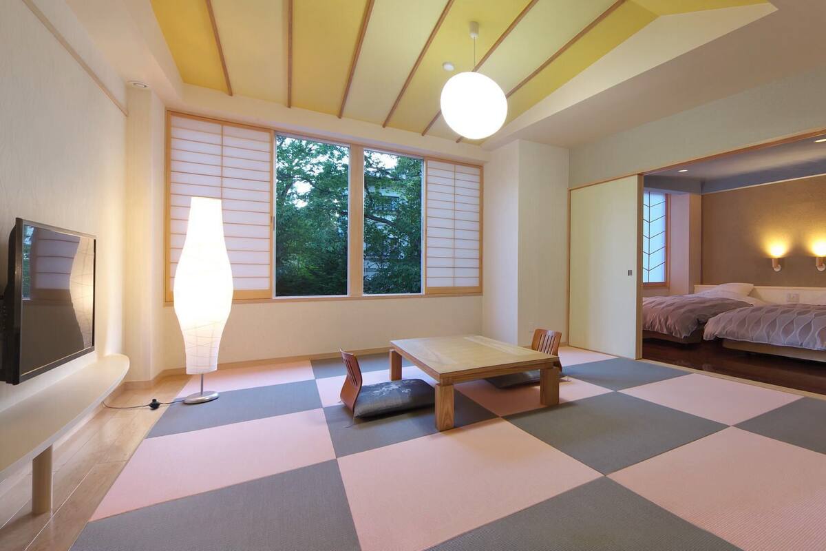 Quarto com esteiras de tatame, uma cama, uma televisão e uma porta deslizante para outro cômodo.