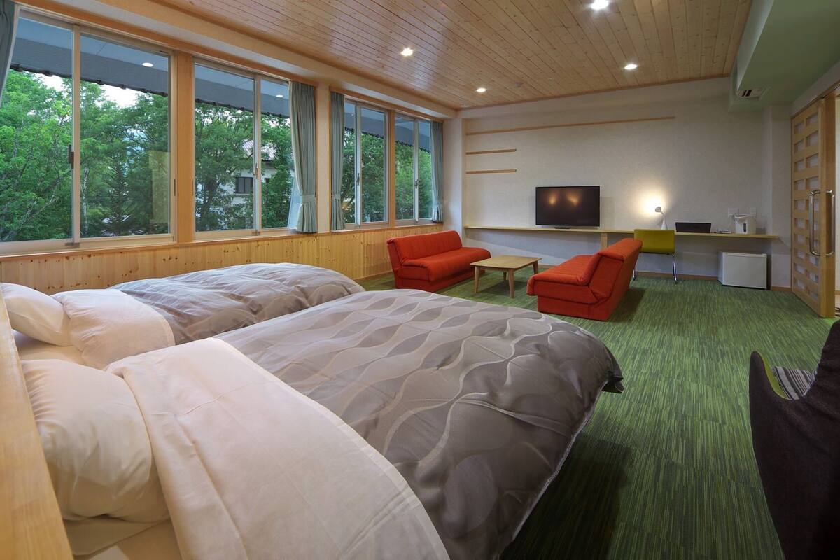 Quarto de hotel com duas camas, televisão, escrivaninha e vista para árvores.