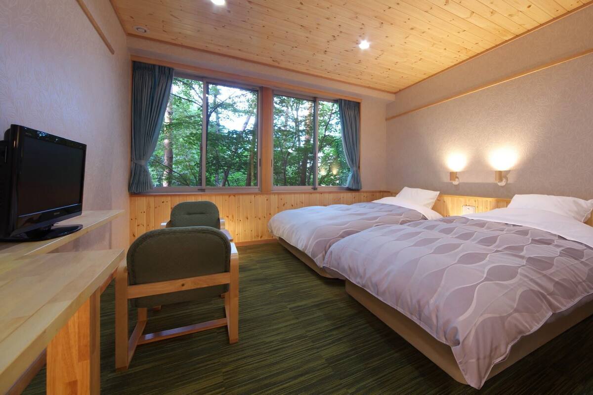 Quarto com cama, cadeira, televisão e janelas com cortinas.