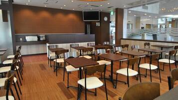 Restaurante com piso de madeira, mesas e cadeiras dispostas para refeições.