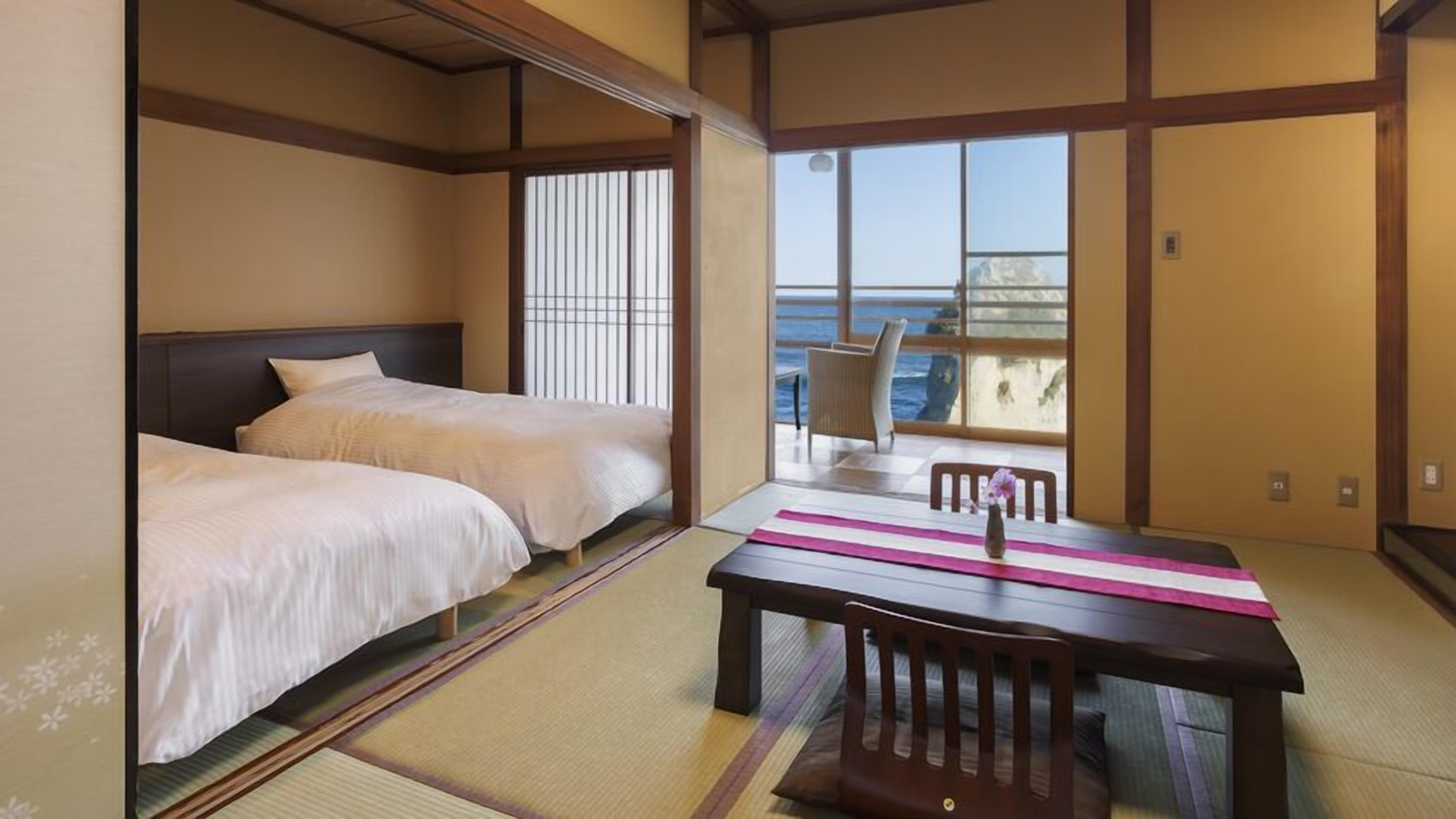 Quarto japonês tradicional com tatames, duas camas, uma mesa com um vaso e vista para o mar.