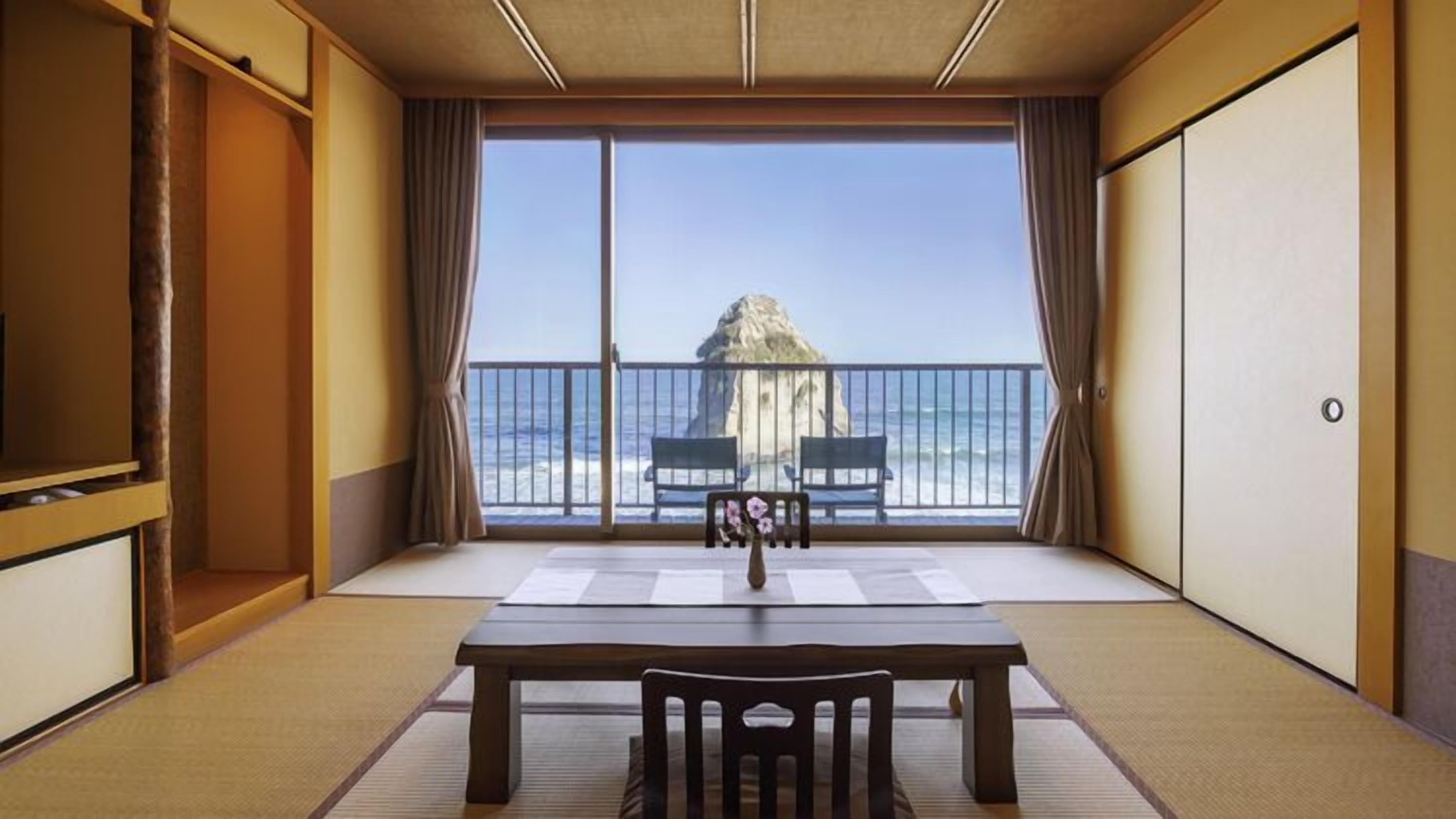 Um quarto com piso de tatame, uma mesa baixa e vista para o mar.
