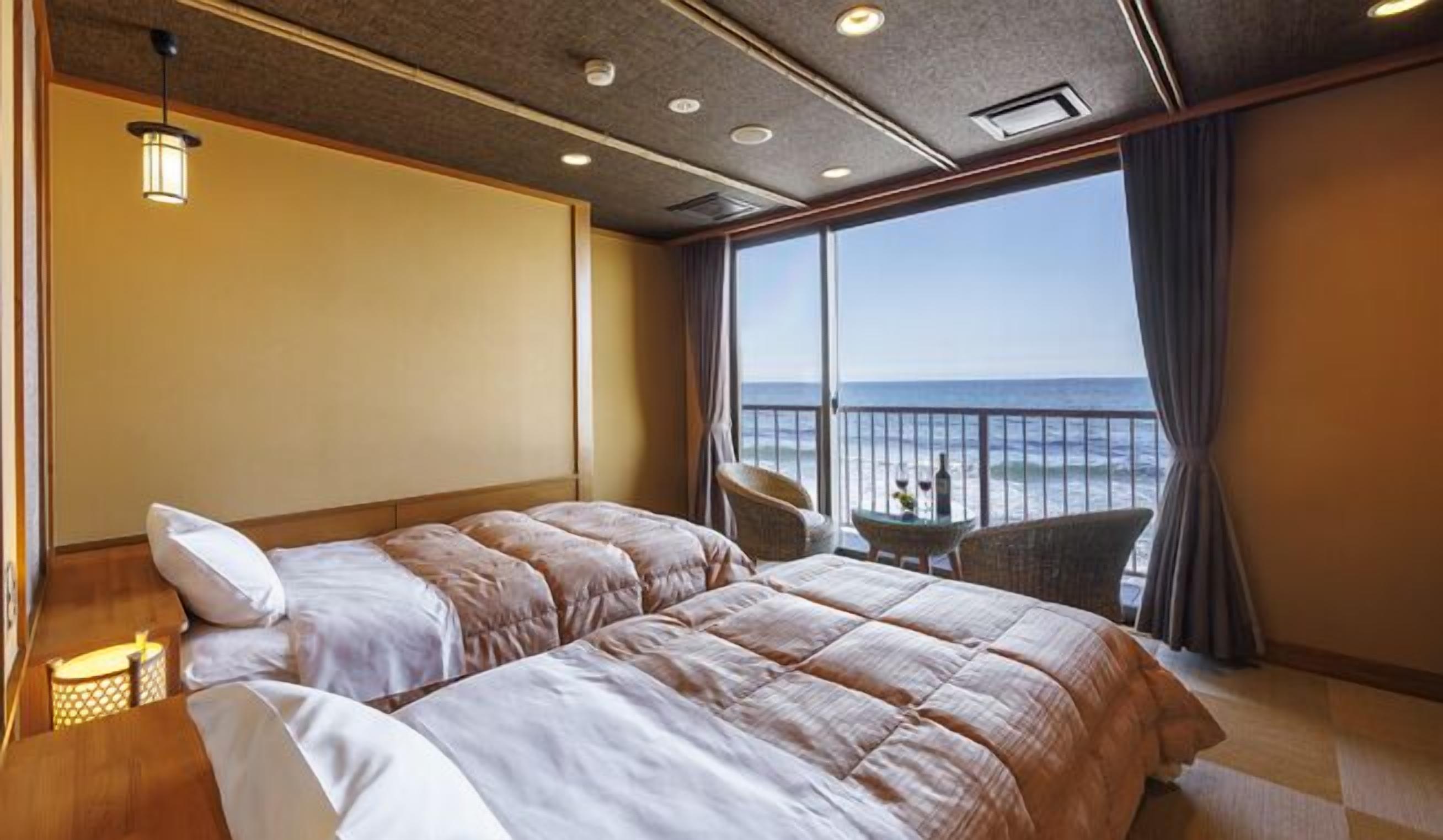 Quarto de hotel com uma cama grande, uma mesa pequena com duas cadeiras e vista para o oceano.