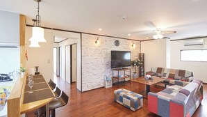 Uma sala de estar moderna com uma mesa de jantar de madeira, um sofá e uma TV fixada em uma parede de tijolos.