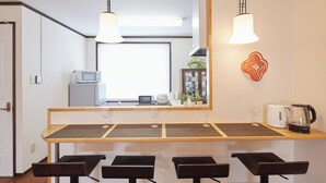 Uma cozinha compacta com bancada de madeira, quatro banquetas, um micro-ondas e uma chaleira.