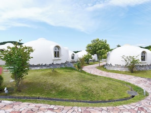 Uma série de edifícios em forma de cúpula com alicerces de pedra, rodeados por jardins bem cuidados e um caminho pavimentado.