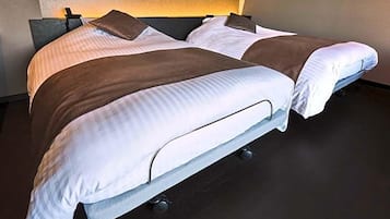 Uma cama de casal com cabeceira escura, roupa de cama branca e castanha, e uma pequena mesa de cabeceira com uma luminária.